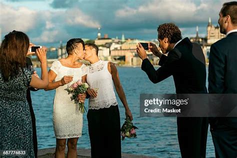 Happy Man Standing With Friends While Photographing Lesbian Couple Kissing At Wedding High-Res ...