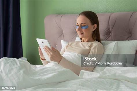 침실 내부의 침대에서 태블릿을 사용하여 얼굴에 패치를 붙인 아름다운 젊은 여성 30 34세에 대한 스톡 사진 및 기타 이미지 30 34세 가정의 방 감정 Istock