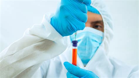 백색 배경에 주사기가 있는 시험관에서 샘플을 채취하는 생체 보호 복 얼굴 마스크 및 파란색 장갑을 착용한 라틴 의사의 모습을