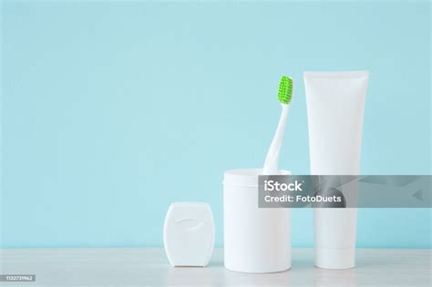플라스틱 유리에 녹색 강 모가 있는 칫 솔 치약의 흰색 튜브 및 파스텔 블루 벽에 선반에 치 실을 컨테이너 치아 위생 텍스트