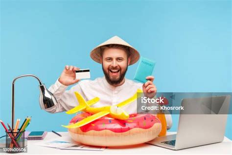 고무 반지와 장난감 비행기로 직장에 앉아 여권과 신용 카드를 들고 해외 휴가를 계획하고 티켓을 예약하는 행복한 긍정적 인 남자
