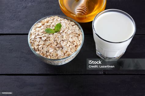 오트밀 꿀 및 우유입니다 귀리 플레이크 우유와 꿀 나무 막대기로 유리 검은 나무 보드에 아침 식사 오트밀입니다 건강 한 음식입니다 미니 0명에 대한 스톡 사진 및 기타