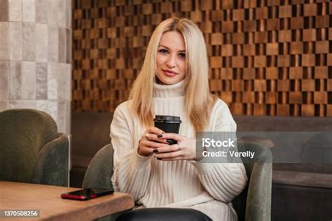 실내 카페에 앉아 커피 한 잔을 들고 미소 짓는 중년 여성 흰색 스웨터에 백인 소녀 금발 머리에 대한 스톡 사진 및 기타 이미지 금발 머리 낮 도시 Istock