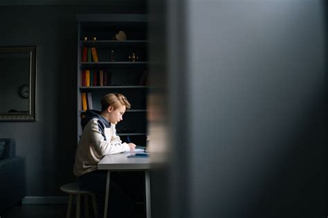 학생 소년은 펜과 복사책에 메모를하고 어린이 방의 창문 근처 책상에 앉아 노트북 컴퓨터를 사용하여 노트북 사용하기에 대한 스톡