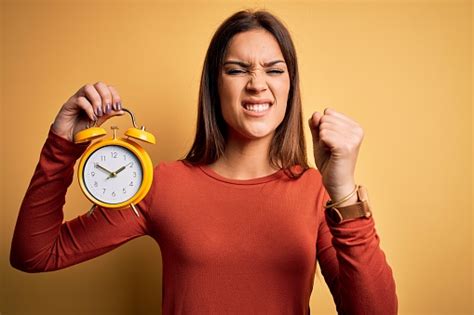 고립 된 노란색 배경에 알람 시계를 들고 젊은 아름다운 갈색 머리 여자는 화가 좌절 고함 미친 고함 으로 제기 된 손 분노 개념 갈색 머리에 대한 스톡 사진 및 기타 이미지