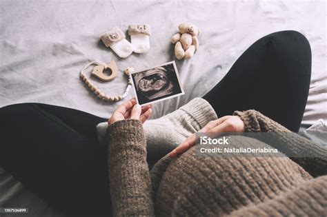 추운 겨울 날에는 초음파 이미지 귀여운 아기 양말 및 장난감을 가진 임산부의 미니멀 한 사진 임신 한 배를 가진 임산부는 아기를 기다리고 있습니다 임신의 개념 양말에 대한