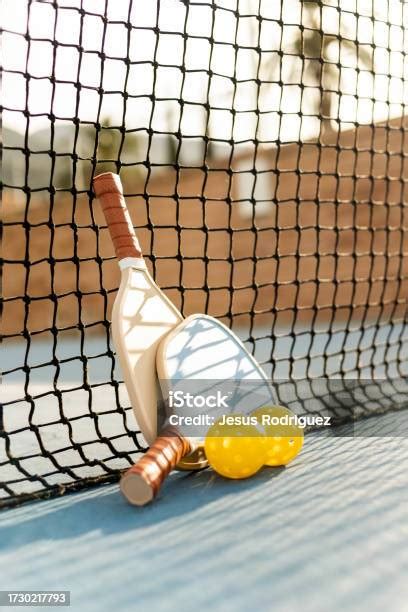 해질녘 스포츠 코트의 네트 옆에 있는 두 개의 피클볼 라켓과 두 개의 공 사진 피클 볼 개념입니다 테니스와 비슷한 스포츠 건강한