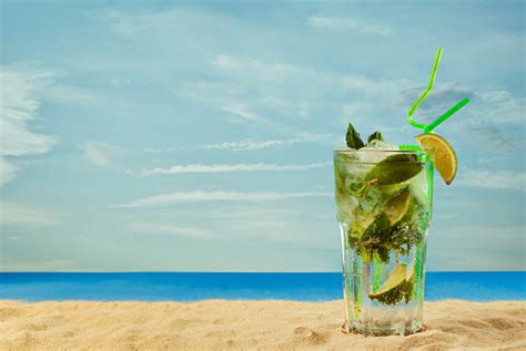 모래 위에 빨대가 달린 녹색 칵테일 해변에서 얼음 라임 민트를 곁들인 알코올 모히토 배경에 일몰 바다와 하늘 유리 근처의