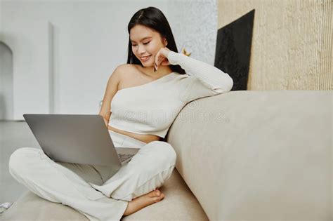 Attractive Asian Woman Using Laptop Computer While Sitting On A Couch