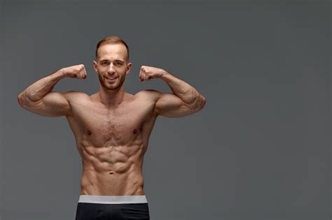 회색 배경에 팔뚝 근육을 과시하는 근육질의 건강한 몸을 가진 잘생긴 젊은 남자 모델의 초상화 프리미엄 사진