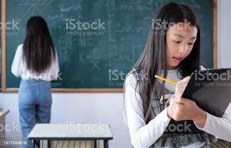 칠판 앞에서 교사와 함께 워크 시트에 글을 쓰는 소녀 학생의 클로즈업 뷰 교실에서 공부하는 학생 의도로 교사로부터 배우는 초등