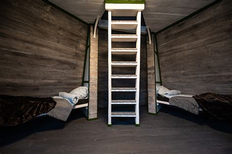 나무 오두막의 틈새에 깨끗한 침구가 있는 싱글 침대 피라미드 모양의 방갈로 여름 집 각진 둘러싸인 벽 흰색 계단 회색 수평 나무 벽 판자 비표준 프레임 구조 0명에 대한