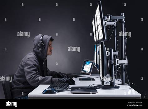 rear view of a hacker using multiple computers for stealing data in