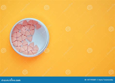 Pink Triangular Unusual Pills In A White Round Box On Yellow Background