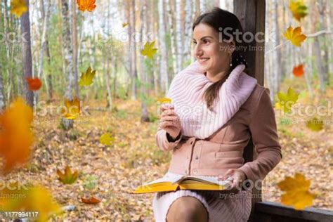 가을 숲에서 소녀 책을 읽고 여자는 가을 숲에서 나무 근처에 앉아 그녀의 손에 책을 보유하고있다 단풍이 배경에 떨어집니다 가을에