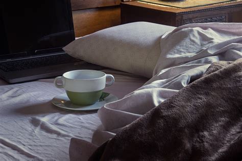 구겨진 담요가 있는 만들어지지 않은 침실 침대에 열린 노트북 옆에 있는 더러운 접시에 빈 머그잔 0명에 대한 스톡 사진 및 기타 이미지 Istock