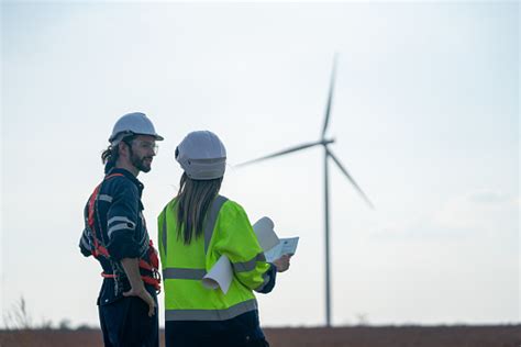 백인 엔지니어 남자와 여자의 뒤는 여자와 함께 그림 종이를 들고 푸른 하늘이 있는 풍차 또는 풍력 터빈의 줄 앞에 머물러 있습니다 지속가능 에너지에 대한 스톡 사진 및 기타