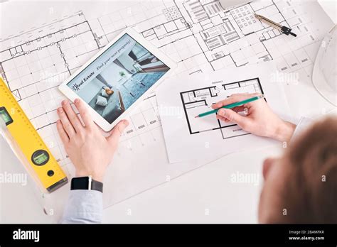 Above View Of Architect Using Digital Tablet And Blueprints While Working On Floor Plan Of Flat