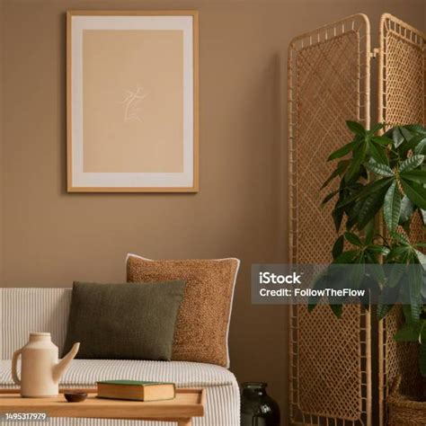 모의 포스터 프레임 베이지색 모듈식 소파 갈색 베개 보헤미안 스툴 칸막이 벽 바구니에 담긴 식물 및 개인 액세서리가 있는 거실 인테리어의 창의적인 구성 가정 장식 템플렛