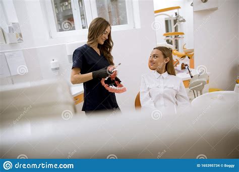 Young Female Dentist Explaining To Female Patient Cleaning Tooth