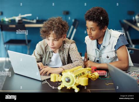 Portrait Of Two Teenage Boys Using Laptop And Programming Robot During Engineering Class In