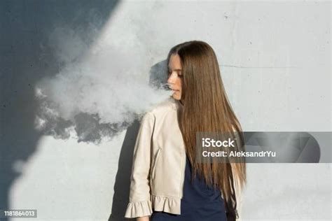 Vape 십대 캐주얼 한 옷을 입은 어린 귀여운 소녀가 여름날 야외 벽 근처에서 전자 담배를 피울 수 있습니다 나쁜 습관 18
