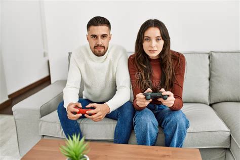 Young Hispanic Couple Playing Video Game Sitting On The Sofa At Home