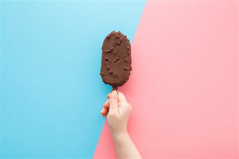 밝은 분홍색 파란색 테이블 배경에 견과류와 초콜릿 유약을 가진 아이스크림을 들고 있는 아기 손 파스텔 색상 근접 촬영 여름에는 어린이차가운 달콤한 간식 하향 보기 쌍방