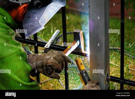 A Welder Wearing A Safety Helmet And Gloves Is Welding A Metal Fence