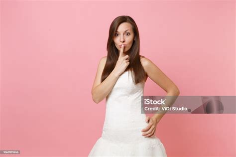 화이트 레이스 웨딩 드레스 핑크 파스텔 배경에 고립 된 입술에 검지 손가락을 유지와 서 아름 다운 신부 여자의 초상화 결혼식 축 하 개념입니다 광고에 대 한 공간을 복사