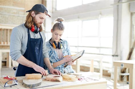 진지 하 게 집중 된 소식통은 모자에 책상에 서 있는 뚜껑을 하 고 전시 인턴 나무와 함께 작업 하는 방법 젊은 여자 나무를 폴란드어 하는 방법을 보고 스케치 북에서 노트