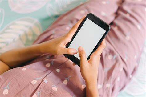 잠옷을 입은 여자의 손이 하얀 화면이 있는 스마트폰을 보며 침대에 누워 있다 스트리밍 레저 개념 Brand Name Smart