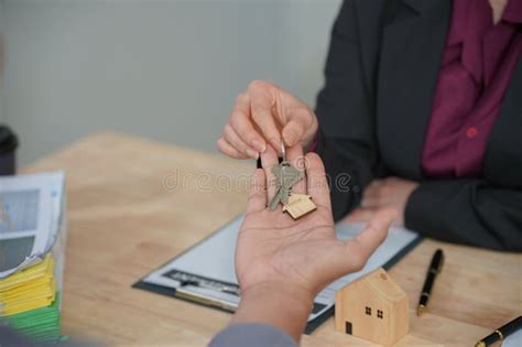 Real Estate Agent Holding House Model And Pen Discussing Contract Terms