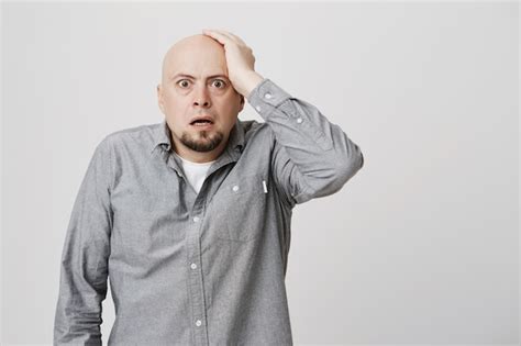 Обеспокоенный озадаченный лысый мужчина держится за голову и смущенно смотрит Бесплатно Фото