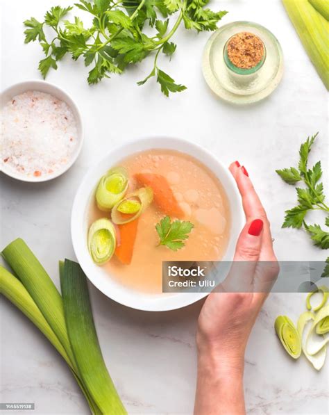 흰색 바탕에 파슬리 부추 월계수 잎 후추를 곁들인 여성들의 손에 칼로겐 그릇으로 가득 찬 기본 뼈 국물 뜨거운 요리법을위한 겨울 기지 수프 리조또 파스타 및 소스 상위 뷰