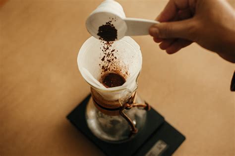 필터에 접지 커피를 붓는 손 대체 커피 양조 V60준비 저울에 부어 유리 주전자의 배경에 갈기 커피와 숟가락을 들고 사람 가루로