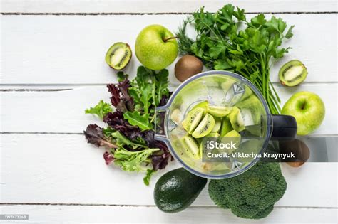 사과 키위 아보카도 양상추 브로콜리 딜 파슬리로 만든 건강한 녹색 스무디를 위한 재료로 흰색 나무 테이블에 있는 믹서기 유리 그릇 주위 맨 위 보기 블렌더에 대한 스톡 사진