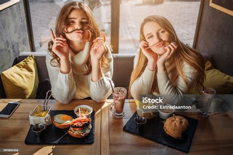 재미 있은 젊은 여자는 카메라에 포즈 봐 그들은 코와 입술 사이 머리의 조각 잡아 모델 재미가 있다 그들은 내부 테이블에 앉는