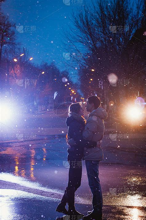 相爱的情侣在夜晚城市街道的雪中接吻