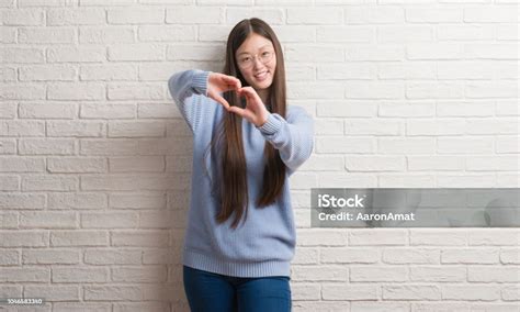 젊은 Chinise 심장 기호와 손으로 모양을 보여주는 사랑에 웃 고 흰색 벽돌 벽에 여자 낭만적인 개념입니다 개념에 대한 스톡