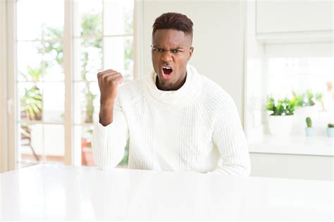 흰색 테이블에 잘생긴 아프리카계 미국인 남자 화가 분노와 소리를 지르는 동안 좌절 주먹과 분노를 제기 분노와 공격적인 개념