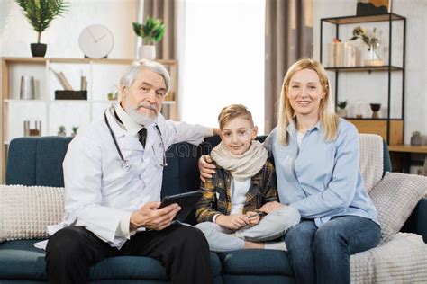 Supportive Attentive Male Doctor Visits Sick Boy Patient At Home Sitting With Mom Stock Photo
