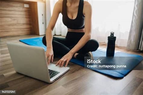 스포츠웨어를 입은 스포티 한 여성은 아령과 단백질 쉐이크 또는 물 한 병으로 바닥에 앉아 노트북을 사용하고 있습니다 가정의 방에
