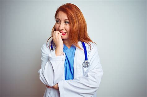 젊은 빨간 머리 의사 여자 는 흰색 고립 된 배경 에 청진기를 사용 하 여 스트레스와 긴장 입 물고 손톱에 손으로 불안 문제 빨간 머리에 대한 스톡 사진 및 기타 이미지
