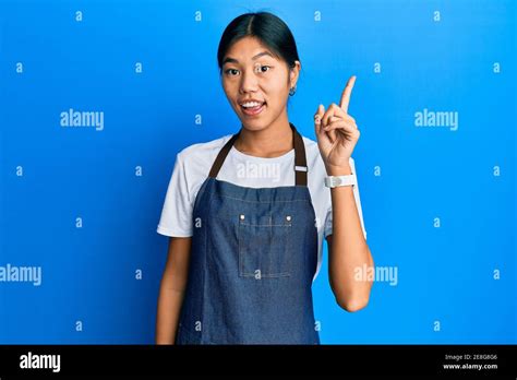 Young Chinese Woman Wearing Waiter Apron Pointing Finger Up With