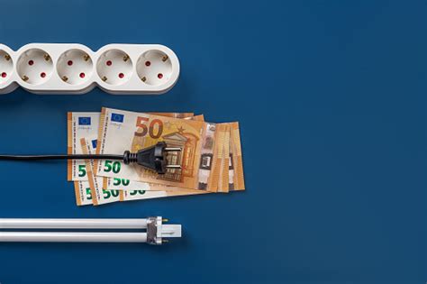 파란색 배경 위에 50 유로 지폐 파워 스트립 및 소형 형광 전구에 전기 플러그 높은 에너지 비용 개념 전기 비용 증가 권력 위기와 인플레이션 멀티탭에 대한 스톡 사진 및