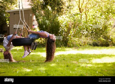 Two Girls Playing Together On Tire Swing In Garden Stock Photo Alamy
