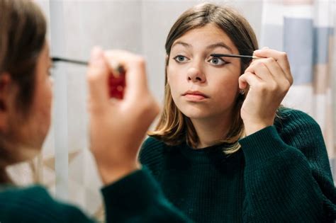 Premium Photo A Girl Paints Her Eyes With Mascara Looking At Herself