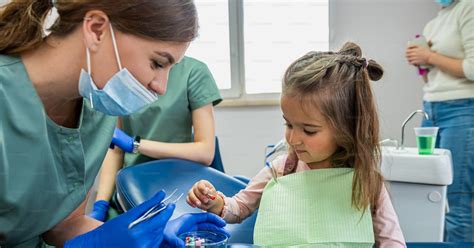 젊은 자격을 갖춘 전문 치과 의사 여성이 리셉션에 데려 온 어린 아이의 치아를 닦고 있습니다 아기 치아 칫솔질의 개념 사진