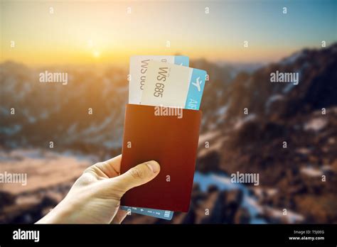 Hand Holding A Passport And Two Air Tickets On A Blue Background Of